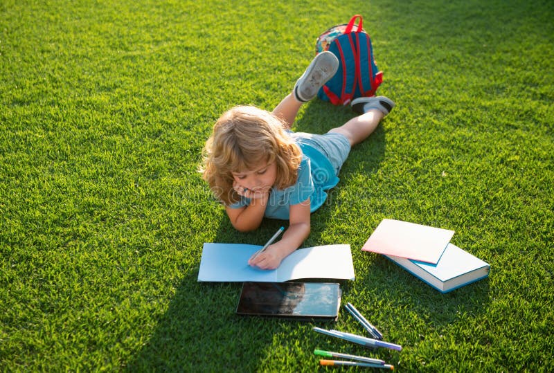 Cute Boy Reading a Book Laying on Grass Writing Notes in Copybook ...