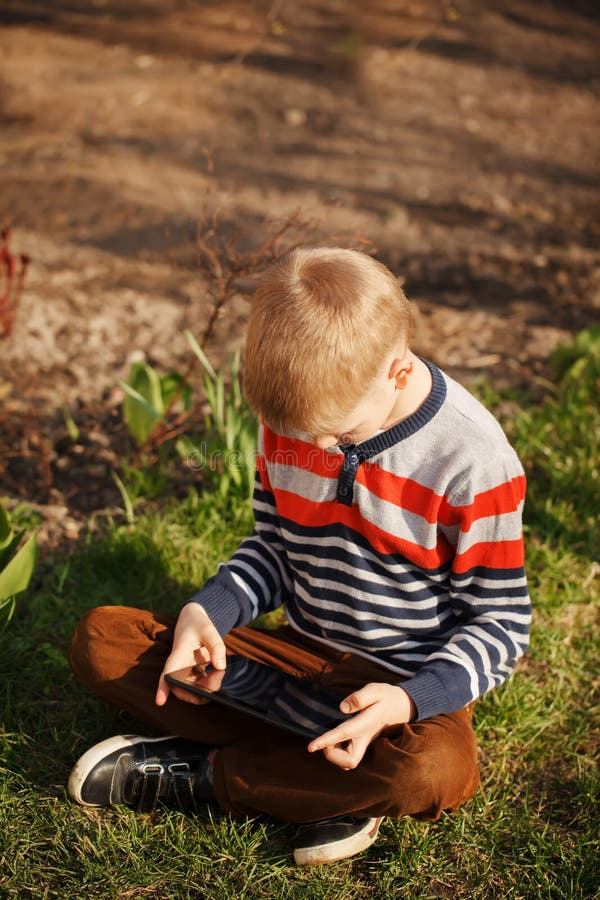 Cute Boy Sitting on Grass in Park and Playing with Tablet Stock Image ...