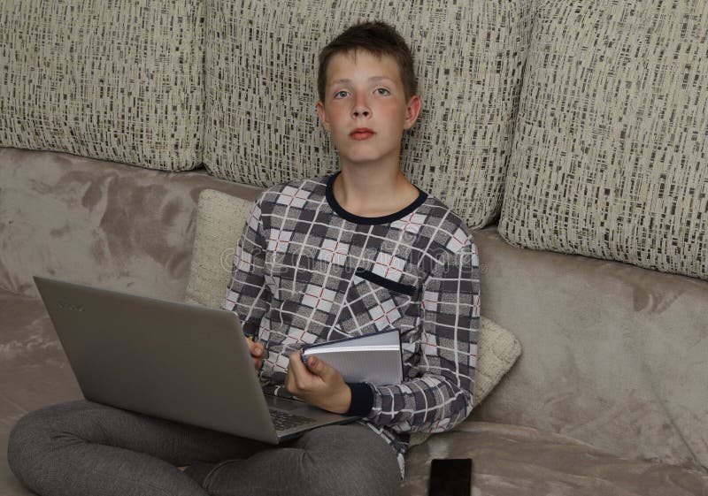A Cute Boy Sitting on the Sofa with a Laptop and a Notebook. Stock ...