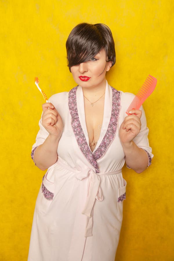 Cute Chubby Girl In A Pink Robe Stands With A Comb And Toothbrush On A