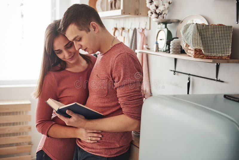 Cute Couple Reading Book Together At Home In The Kitchen At Daytime