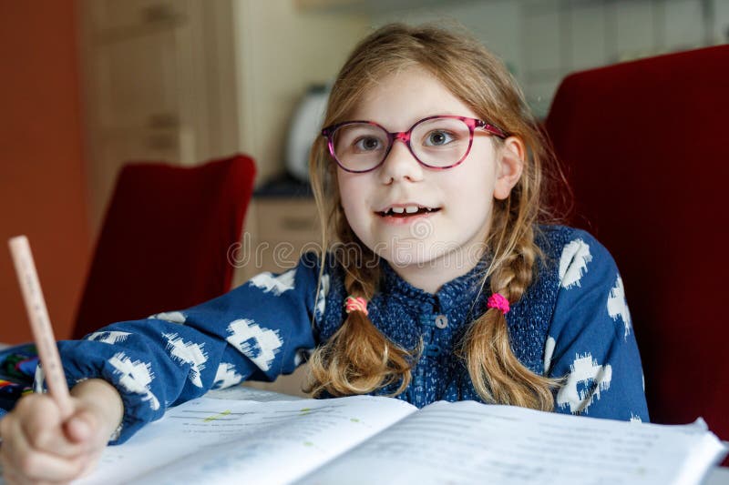Cute Elementary School Girl Sitting at a Desk at Home, Writing in Her ...