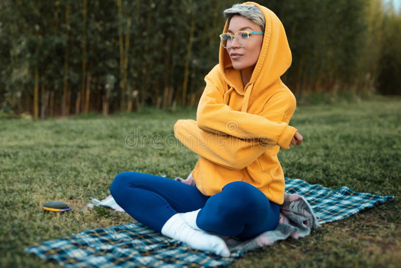Cute Girl With Glasses In An Orange Hoodie Is Sitting In A Park In