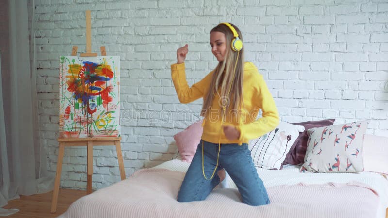 Cute Girl Is Having Fun Dancing On Bed At Home Listening To Music With