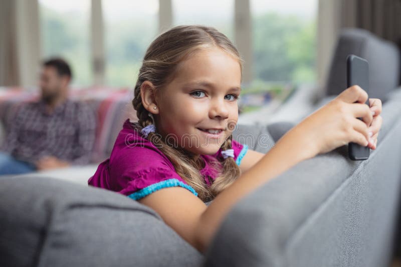 Cute Girl Looking at Camera while Using Mobile Phone on Sofa in a ...