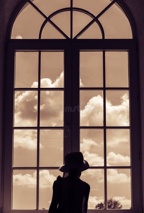 Cute Girl Stands Near A Window And Looks At The Sky With Clouds Stock