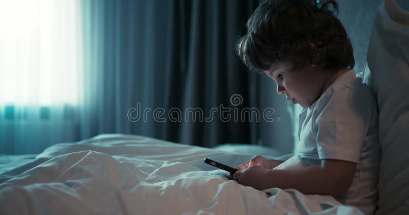 Cute Little Boy Seated Alone in Bed Attentively Watching a Video. Stock ...