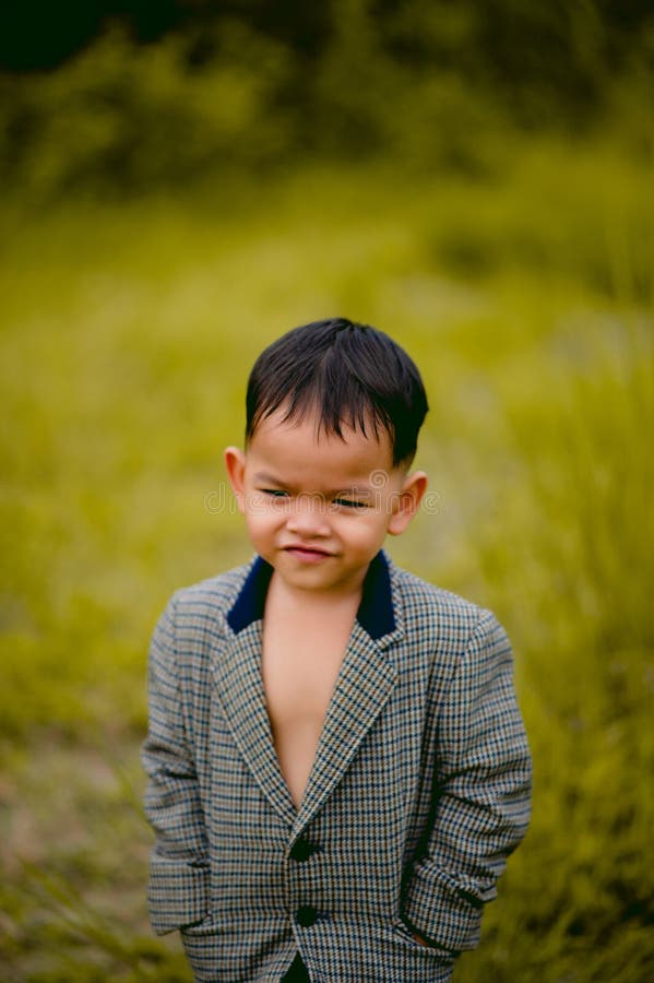 Little Boy a Well-dressed Boy in a Suit in a Backyard with a Lawn and Looking for Something ...