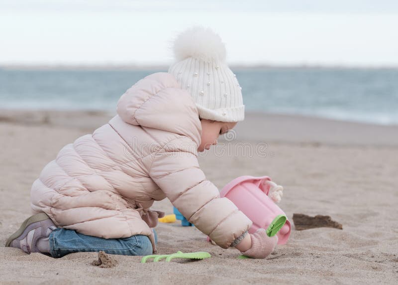 Cute Little Girl is Digging in the Sand on a Cold Day at the Beach ...