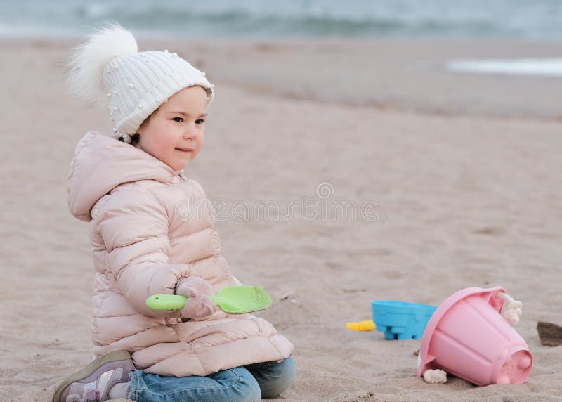 Cute Little Girl is Digging in the Sand on a Cold Day at the Beach ...