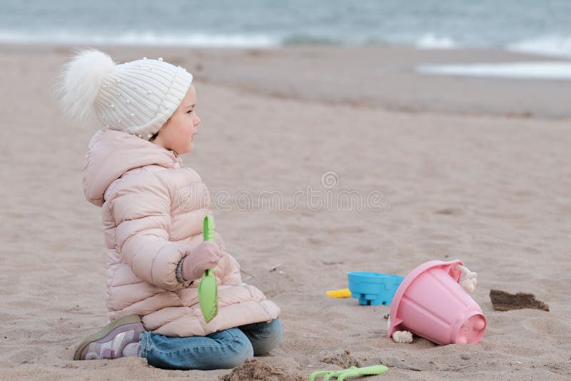 Cute Little Girl is Digging in the Sand on a Cold Day at the Beach ...