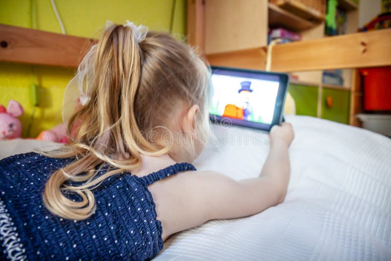 Cute Little Girl Lying on Bed and Using Her Tablet Computer Stock Photo ...