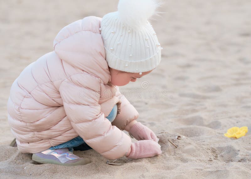 Cute Little Girl is Digging in the Sand on a Cold Day at the Beach ...