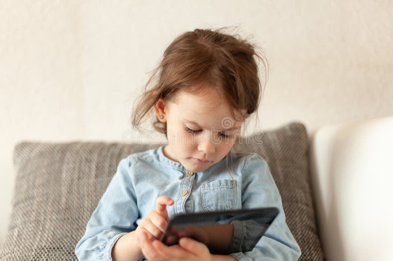 Cute Little Girl Playing with a Tablet on the Sofa at Home Stock Image ...