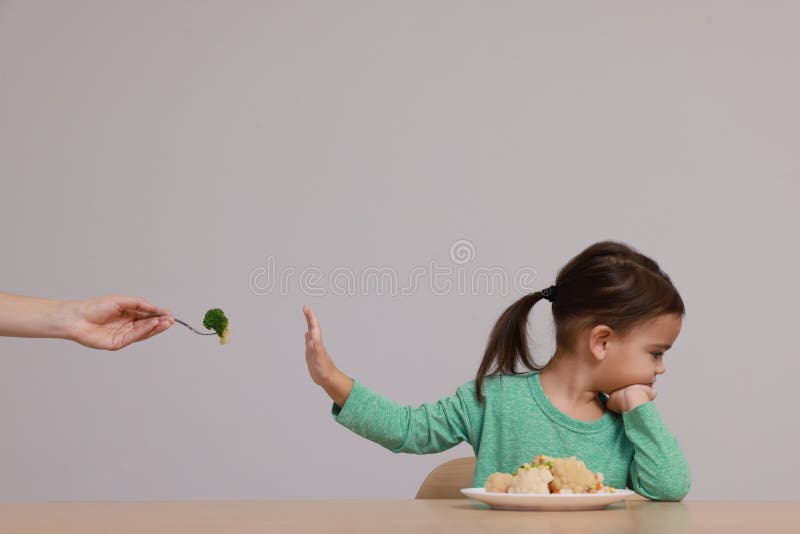 Cute Little Girl Refusing To Eat Vegetables at Table on Grey Background ...
