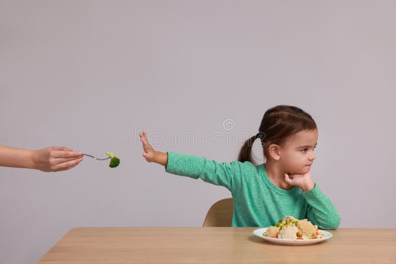 Cute Little Girl Refusing To Eat Vegetables at Table on Grey Background ...