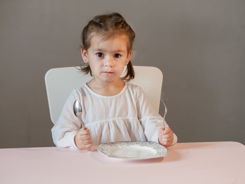 Cute Little Girl Sitting on Table with Plate, Holding Fork and Spoon ...