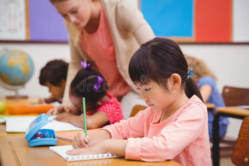 Cute Pupils Writing at Desk in Classroom Stock Photo - Image of learn ...