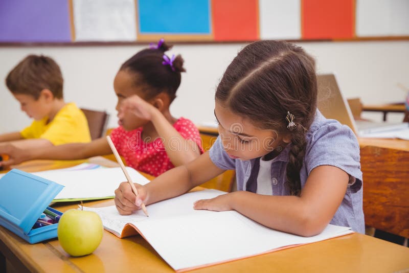 Cute Pupils Writing at Desk in Classroom Stock Photo - Image of ...