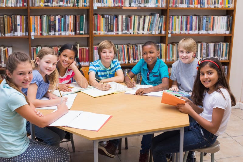 Cute Pupils Writing at Desk in Library Stock Photo - Image of library ...