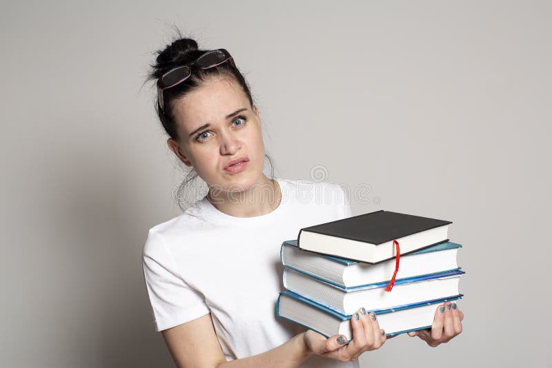 Cute, Puzzled Student with Glasses on Head Holds a Stack of Books in ...