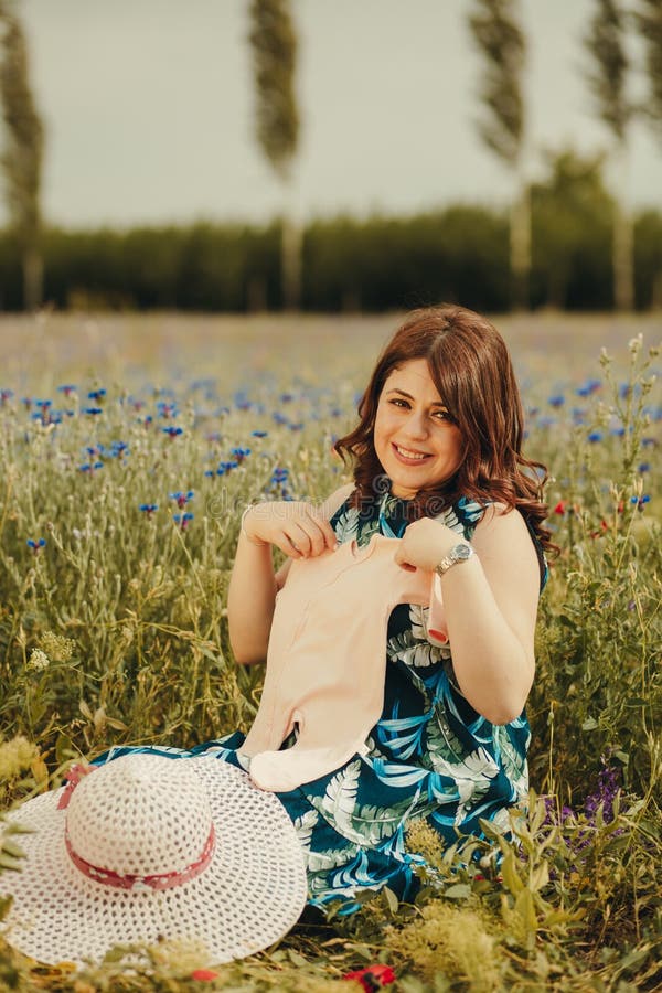 Smiling Pregnant Woman Sitting On Grass And Touching Her Big Belly