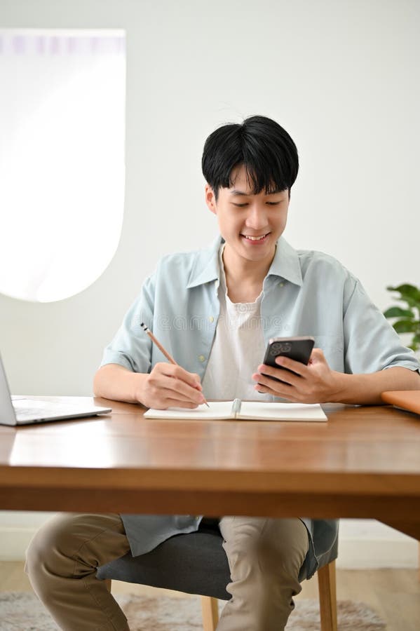Cute Young Asian Male College Student Using His Smartphone while Doing ...