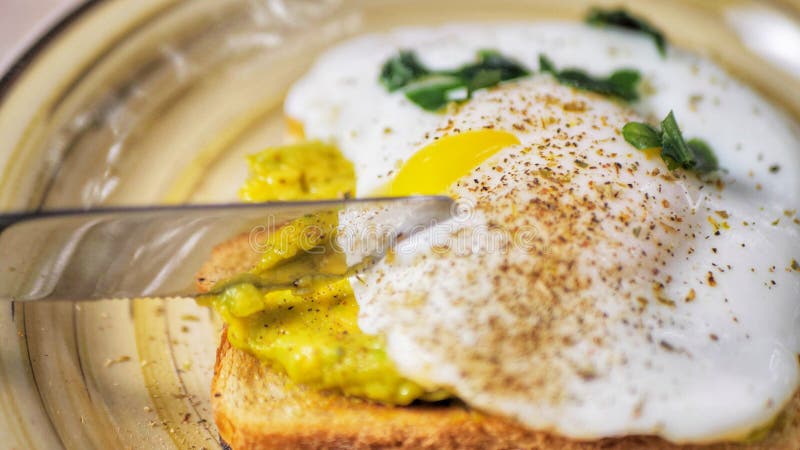 Cutting Poached Egg with Runny Egg Yolk Over Bread Toast with Mashed ...