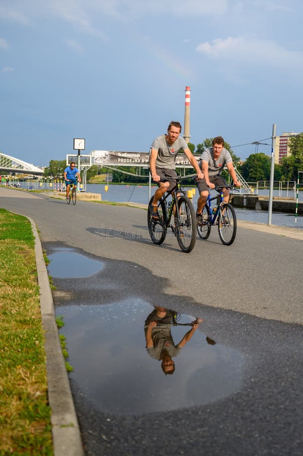 Cyclists on a Riverside Path with Reflection in Water Puddle Editorial ...