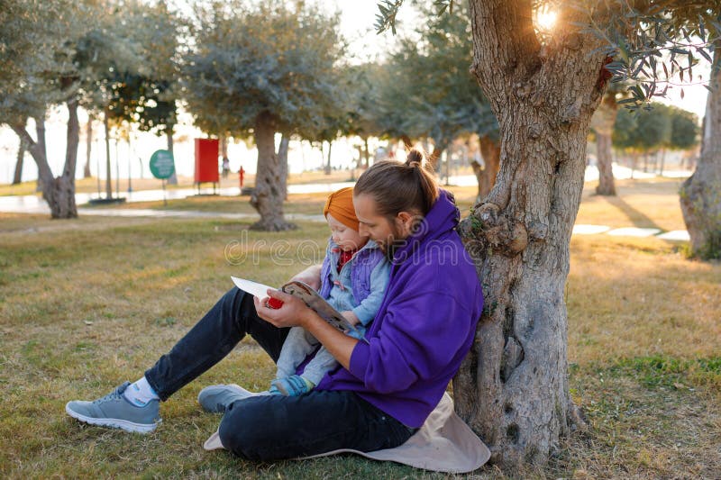 Dad and Baby Read a Book Under a Tree in the Park. Stock Image - Image ...