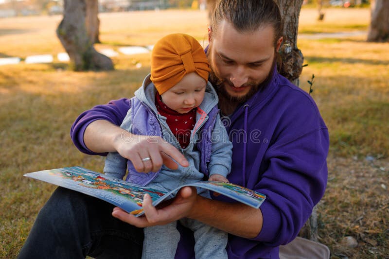 Dad and Baby Read a Book Under a Tree in the Park. Stock Photo - Image ...