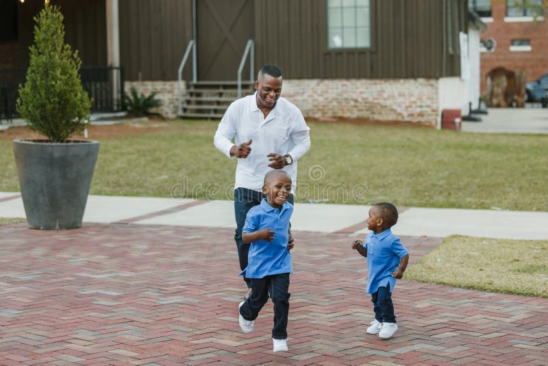 A Dad Chasing His Two Sons Outdoors while they are Playing Together and ...