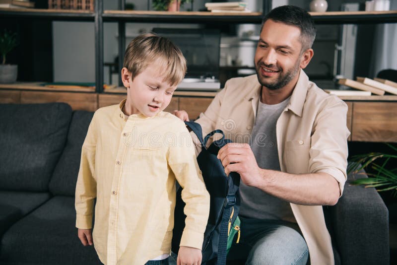 Dad Helping Cute Boy Putting on Backpack at Home Stock Image - Image of ...