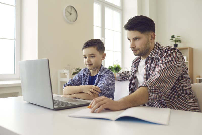 Dad Sits with His Son and Helps Him with His Studies Using a Laptop To ...