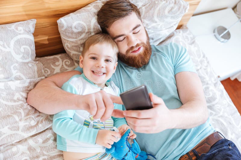 Dad and Son Using Cell Phone on Bed Together Stock Image - Image of ...