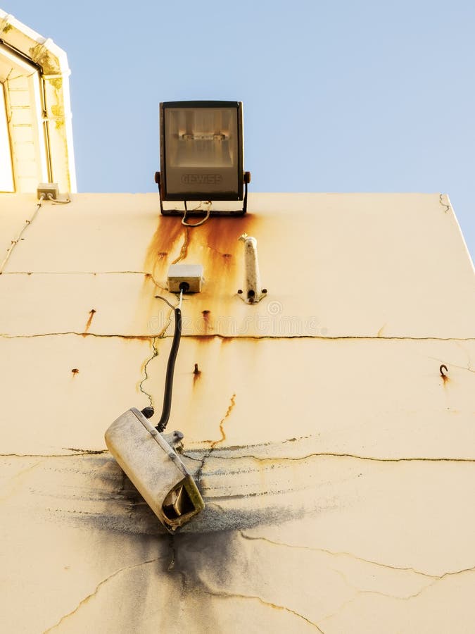 Damaged CCTV Camera Hanging on a Cable on Yellow Wall, Old Flood Light ...