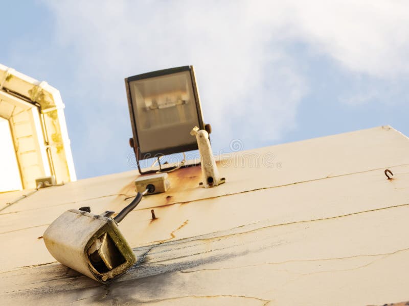 Damaged CCTV Camera Hanging on a Cable on Yellow Wall, Old Flood Light ...