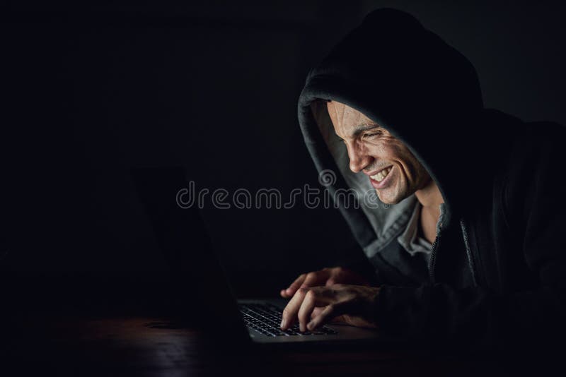 Dark Deeds on a Dark Night. a Hooded Computer Hacker Using a Laptop in ...