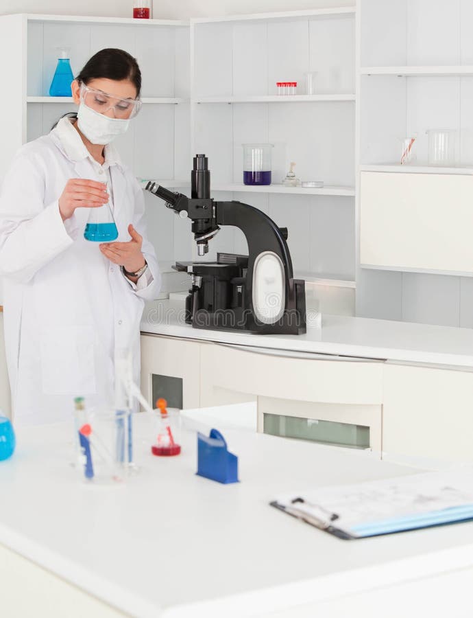 Female Scientist Holding Flask with Blue Solution beside Microscope at ...