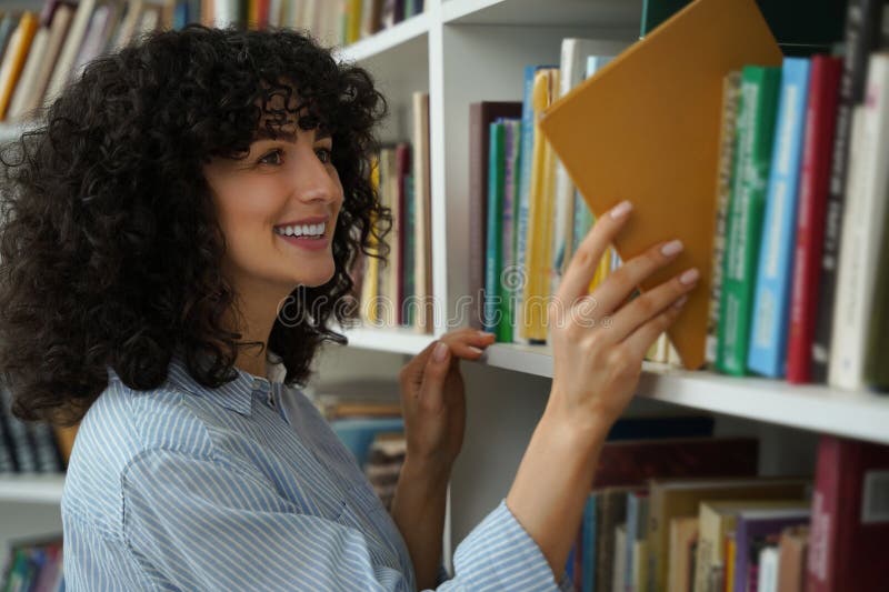 Dark-haired Librarian Taking a Book from the Book Shelve in a Library ...