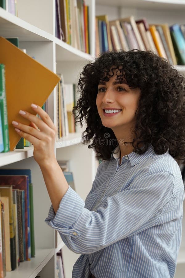 Dark-haired Librarian Taking a Book from the Book Shelve in a Library ...