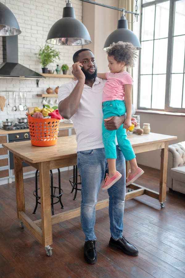 Dark-skinned Tall Father Standing and Holding His Kid while Talking on ...