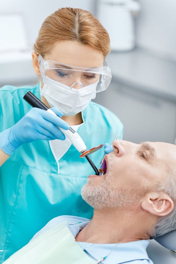 Dentist Using Dental Curing UV Lamp on Teeth of Mature Patient Stock ...