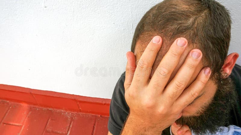 Depressed Young Man Closing His Face with His Hand Sitting by the Wall ...