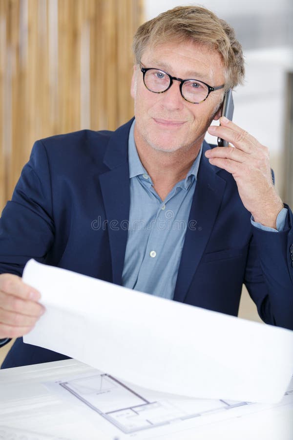 Designer Working on Blueprint in Office and Using Mobile Phone Stock ...