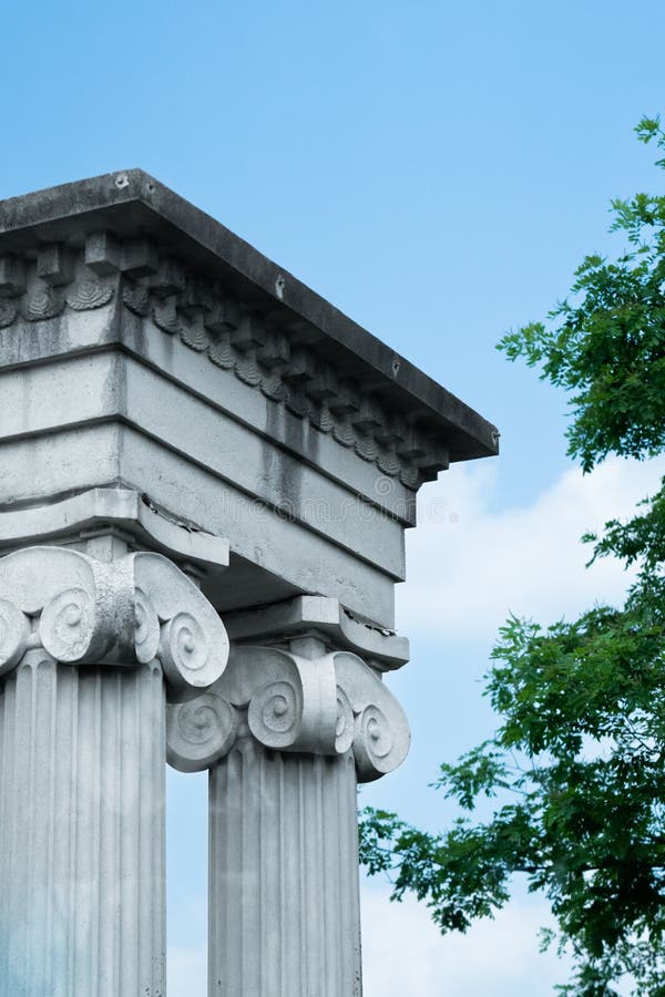 Detailed View of Ionic Column Capitals Against a Blue Sky with Green ...