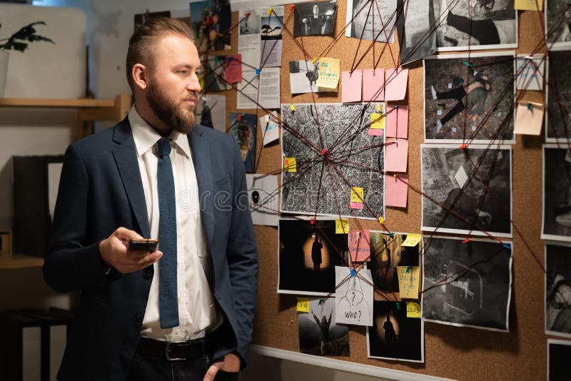 Detective Looking at Evidence Board in Office and Working Using Mobile ...