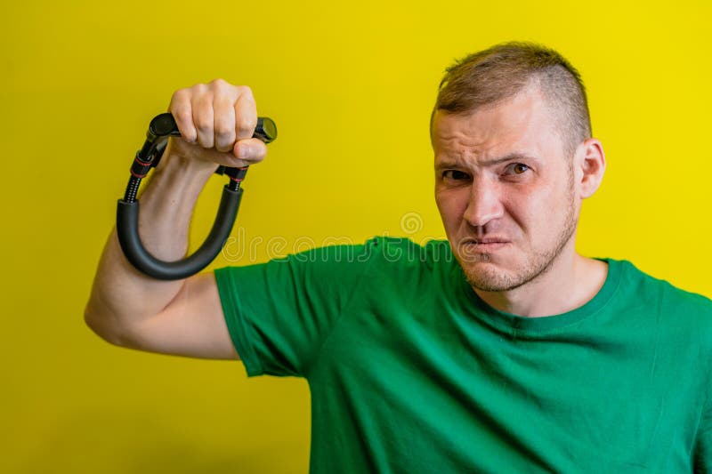 Determined Man Flexing Bicep with Hand Grip Exerciser Against Yellow ...