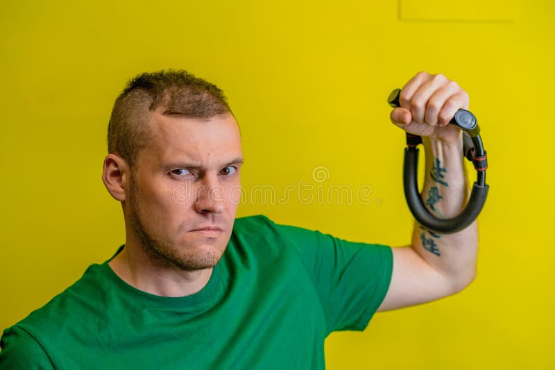 Determined Man Flexing Bicep with Hand Grip Exerciser Against Yellow ...