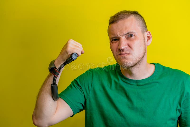 Determined Man Flexing Bicep with Hand Grip Exerciser Against Yellow ...